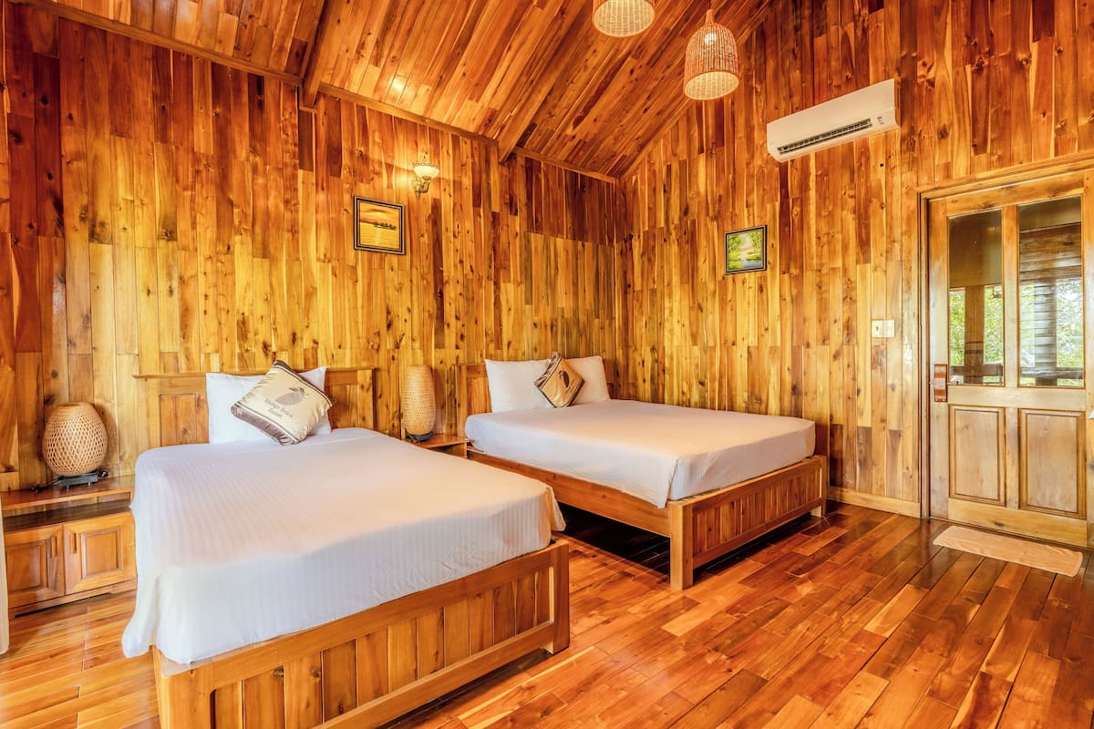 Quarto estilo cabana de madeira com duas camas, piso de madeira e porta com painéis de vidro.