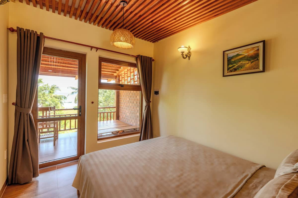 Quarto com cama, varanda com deck de madeira e vista para o verde.