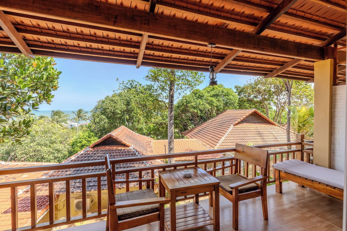 Um deck de madeira com mesa e cadeiras, com vista para uma área residencial com telhados de cerâmica e vegetação exuberante.