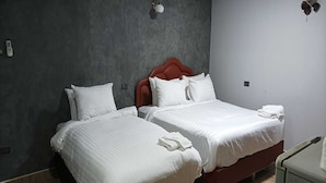 Quarto de hotel com duas camas, cada uma com roupa de cama e almofadas brancas, cabeceira vermelha e uma pequena mesa de cabeceira com abajur.