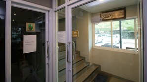 Entrada de hotel com portas de vidro, uma placa indicando concessionária Harley-Davidson e um sinal de pressão nos degraus.