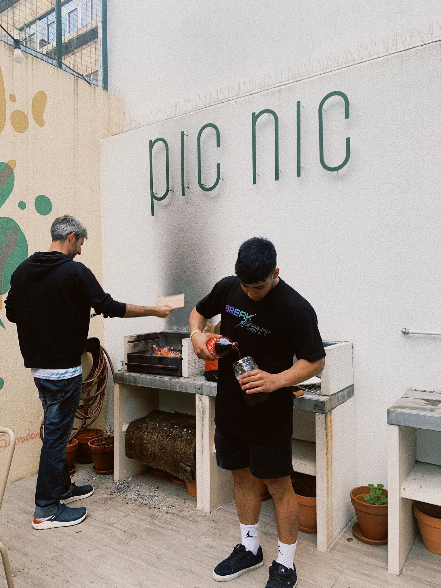 Dois homens num pequeno bar ao ar livre, com um letreiro que diz "pic NIC".