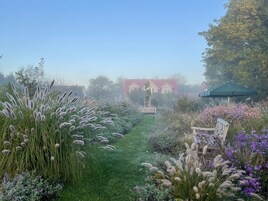 Um caminho de jardim leva a uma casa vermelha com cerca branca e um guarda-sol verde.