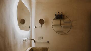 Casa de banho com espelho redondo, prateleira com frascos e porta-toalhas.