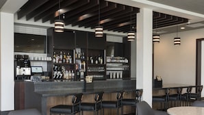 Uma área de bar moderna com balcão, banquetas e iluminação pendente.