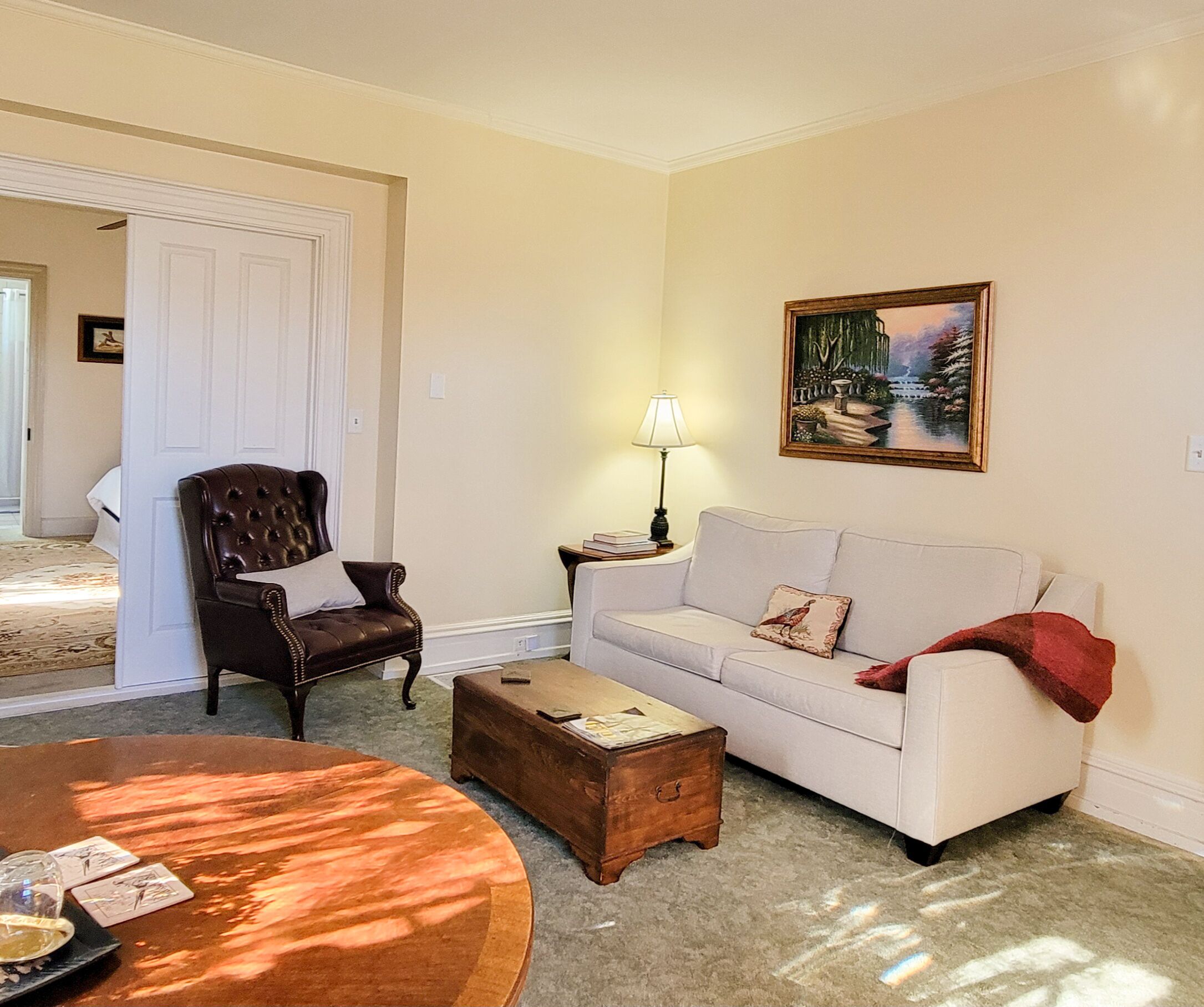 Uma sala de estar com uma poltrona de couro marrom, um sofá branco, uma mesa de centro de madeira e um quadro na parede.