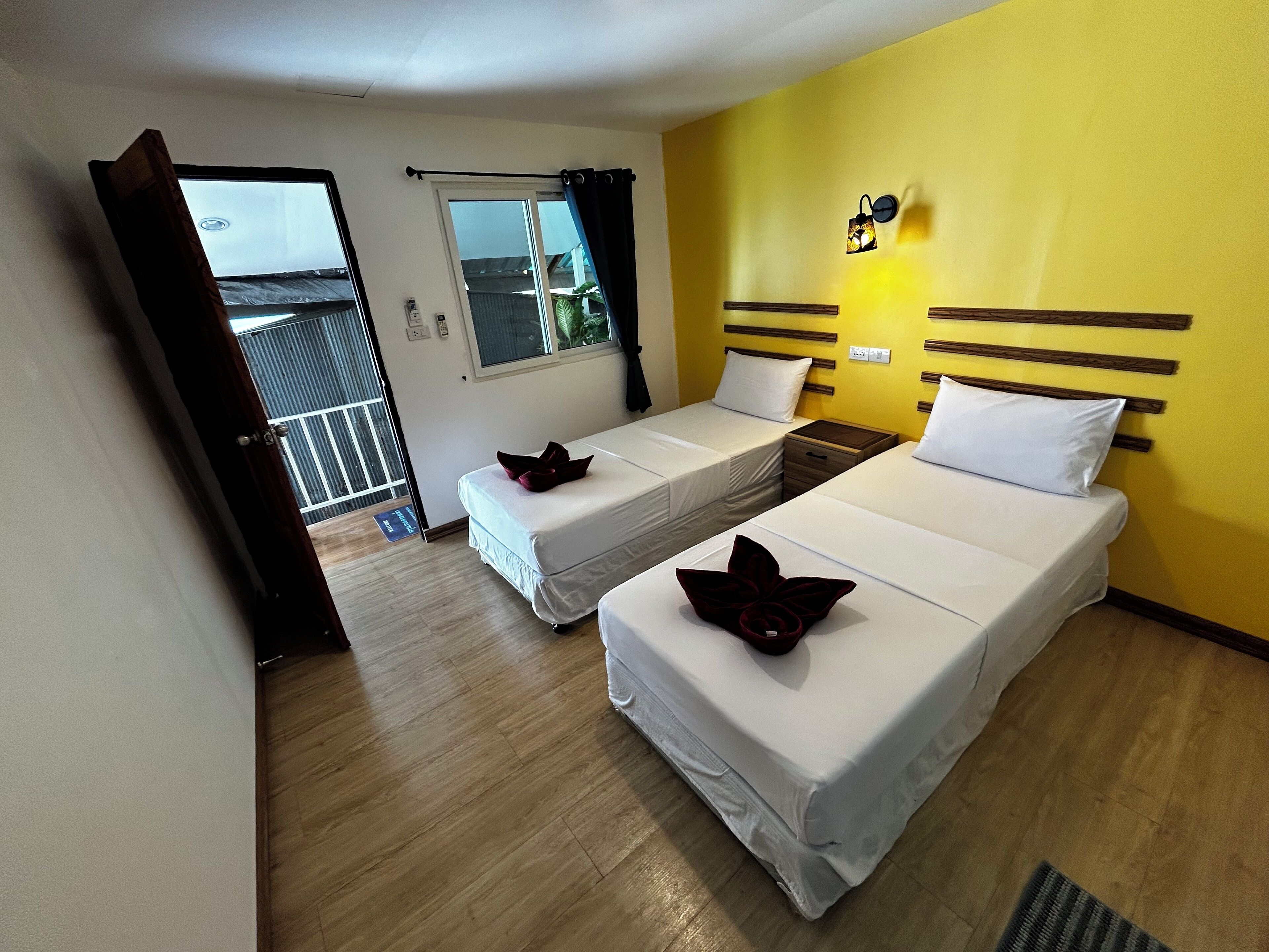 Quarto de hotel com duas camas, uma janela, varanda e parede amarela.