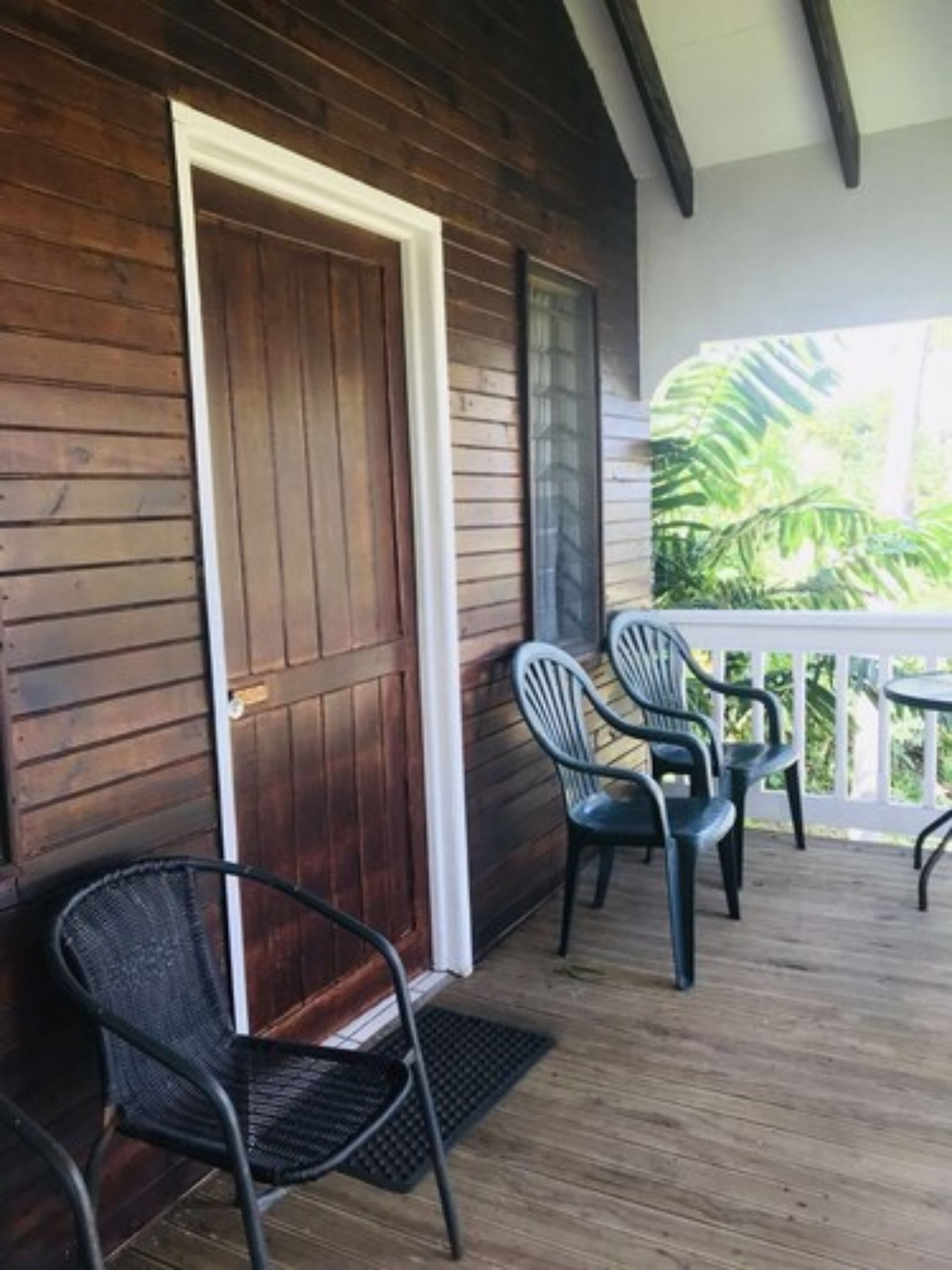 Um alpendre de madeira com uma porta, uma mesa pequena e algumas cadeiras.