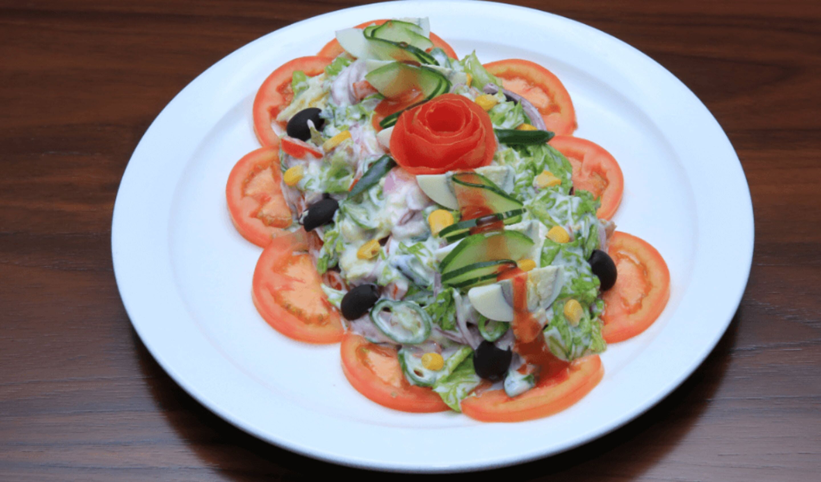 Prato branco com uma salada sobre uma mesa de madeira.