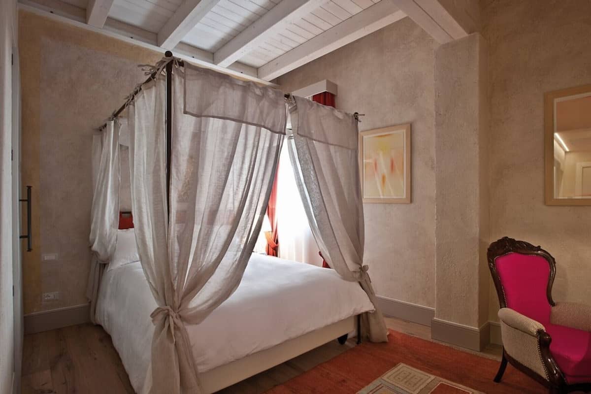 Quarto com uma cama de dossel, uma cadeira e um quadro na parede.