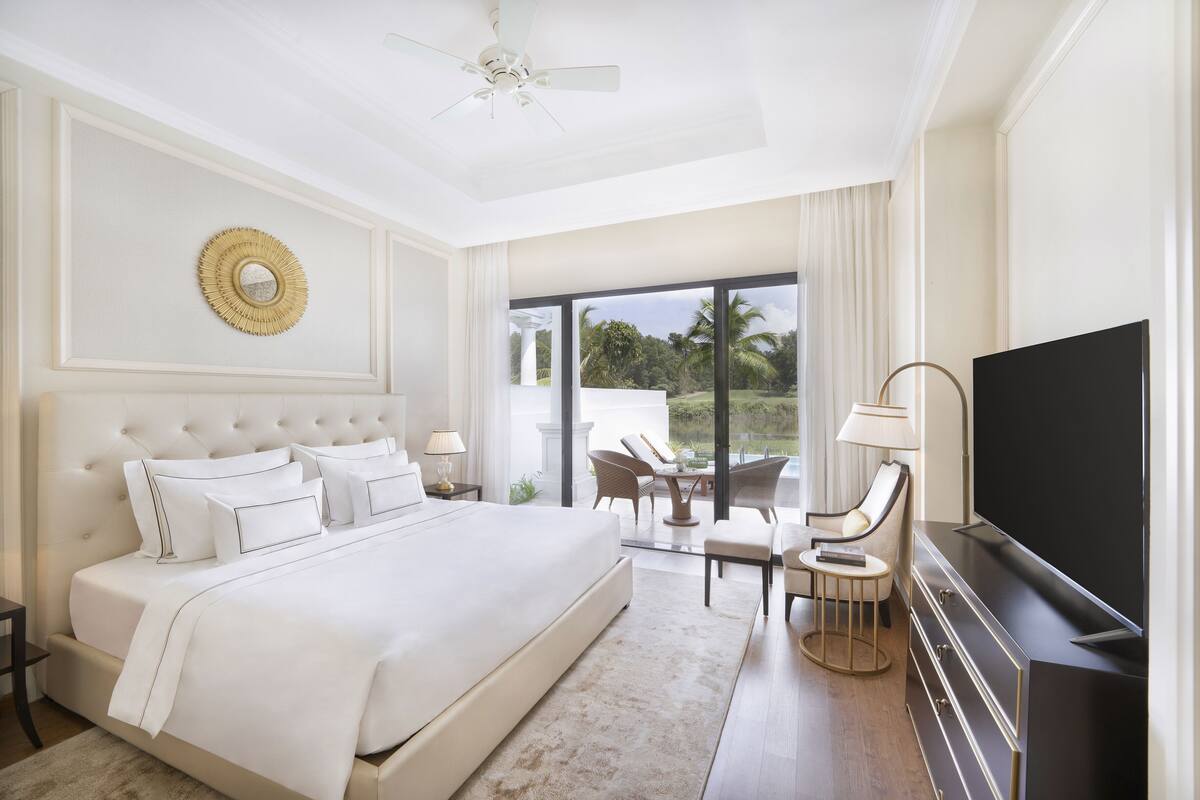 Um quarto espaçoso com uma cama grande, televisão e varanda com móveis de exterior.