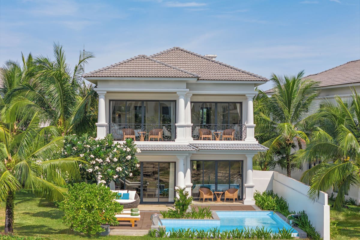 Uma casa de dois andares com varanda, piscina e vegetação exuberante.