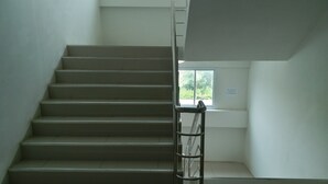 Uma escada com corrimão de metal, uma janela com vista para vegetação e uma placa na parede.