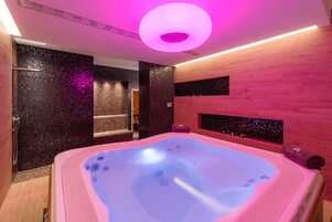 Um spa moderno com uma banheira de hidromassagem grande, paredes de madeira e iluminação ambiente rosa.