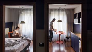 Quarto de hotel com cama, escrivaninha, cadeira, mesa com comida e bebidas, e cozinha.