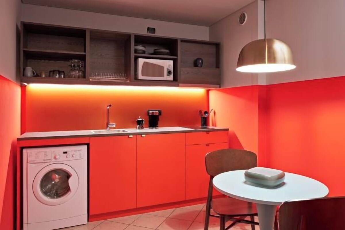 Cozinha compacta com máquina de lavar, micro-ondas e área de jantar com mesa e cadeiras.