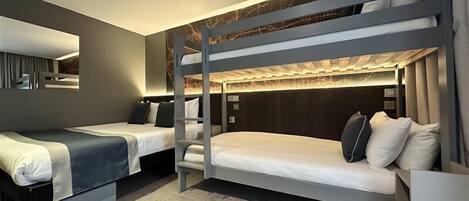 Quarto de hotel com duas beliches, uma escrivaninha e um espelho.
