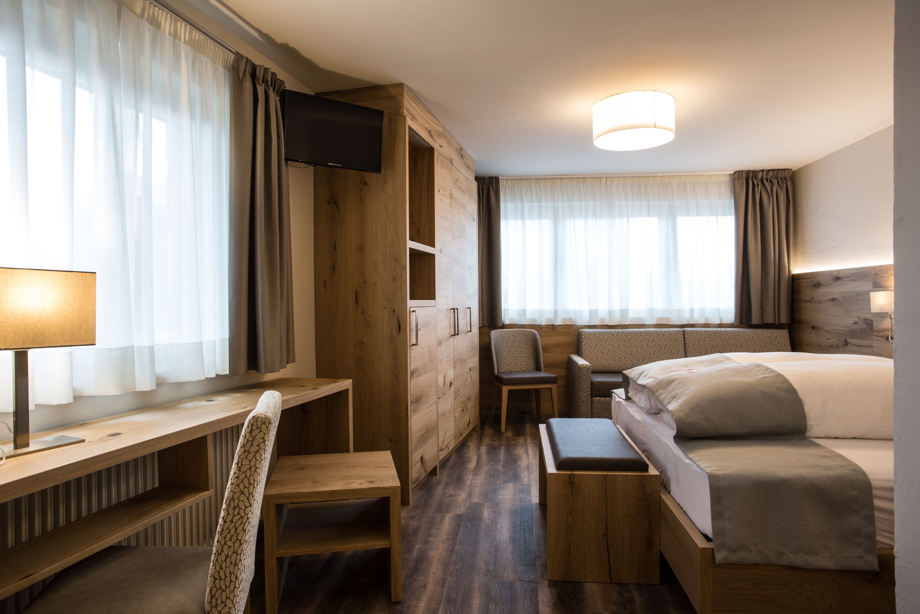 Quarto de hotel com escrivaninha de madeira, cama, cadeira e televisão.