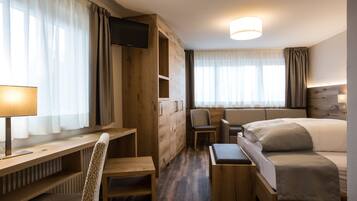 Quarto de hotel com escrivaninha de madeira, cama, cadeira e televisão.