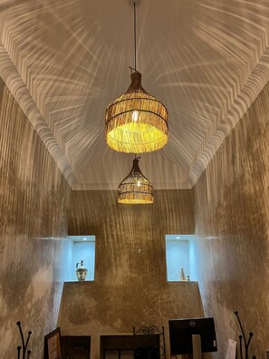 Um quarto com uma luminária pendente grande e trançada, uma escrivaninha com computador e uma tigela decorativa em uma prateleira.