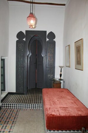 Quarto com piso estampado, cama vermelha, porta decorativa e luminária pendente.