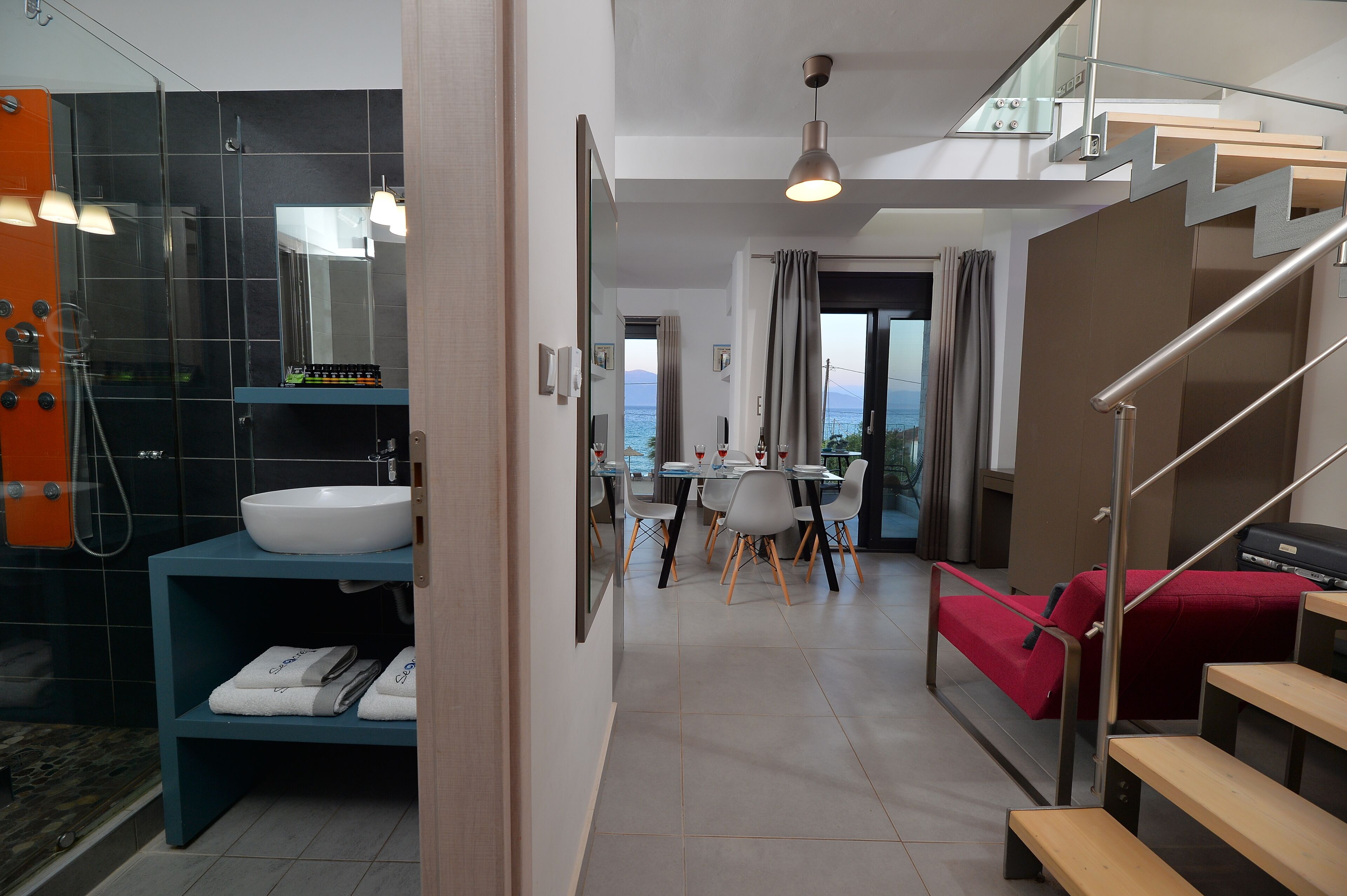 Quarto de hotel moderno com banheiro, área de refeições e vista para o mar.