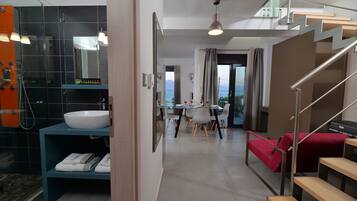 Quarto de hotel moderno com banheiro, área de refeições e vista para o mar.