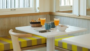 Uma área de refeições com uma mesa, cadeiras e um banco. Há duas tigelas e dois copos na mesa.