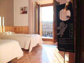 Quarto de hotel com duas camas, chão de madeira e vista para a Praça Los Angeles. Uma placa na porta diz: "PLEASE NO MOLESTEN DO NOT DISTURB NE PAS DERANGER".