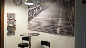 Uma área de refeições com uma mesa redonda e dois bancos altos, um relógio de parede e uma pintura com vista para a cidade.