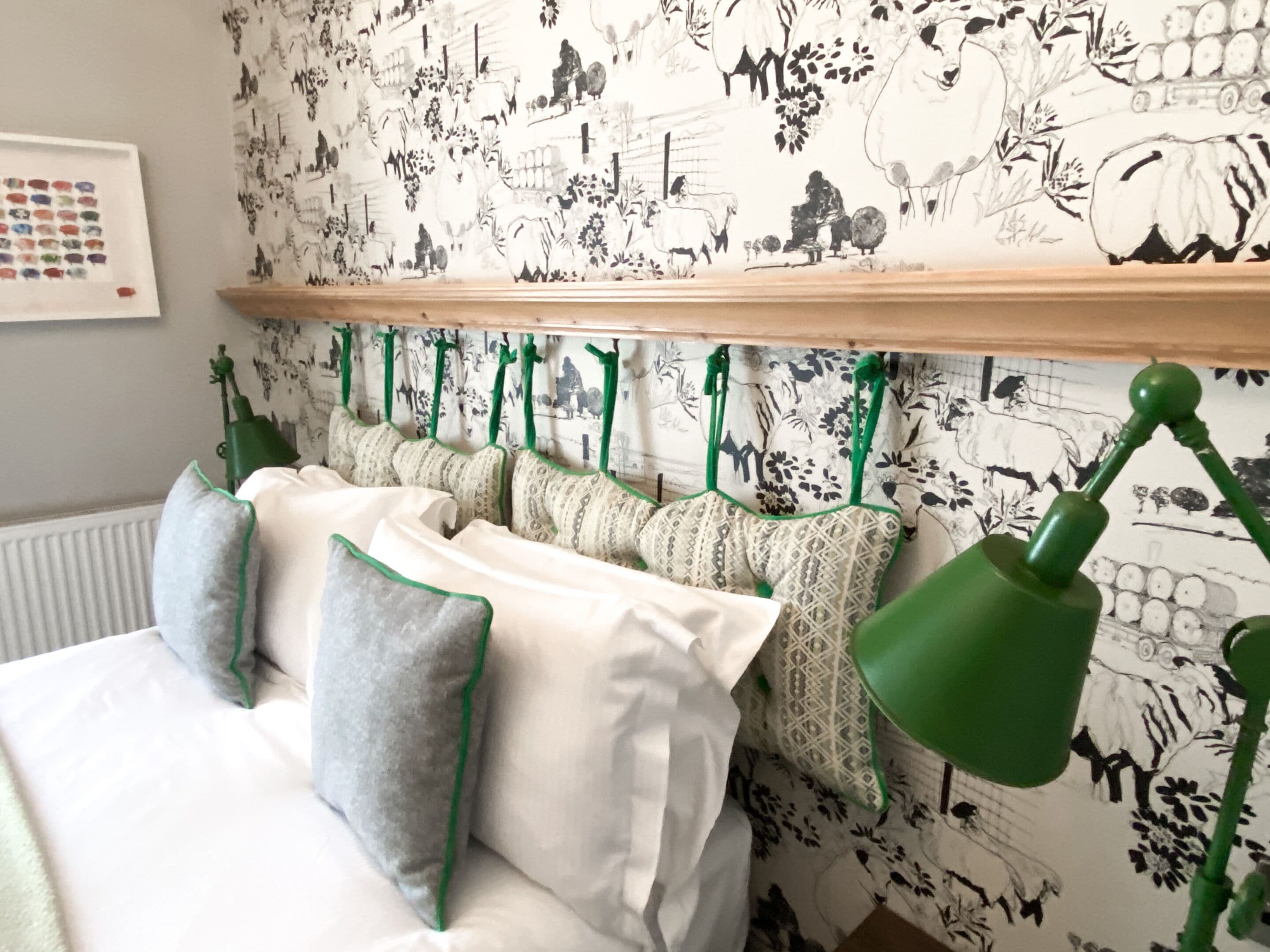 Quarto com cama, almofadas, luminária de chão verde e parede com padrão floral.