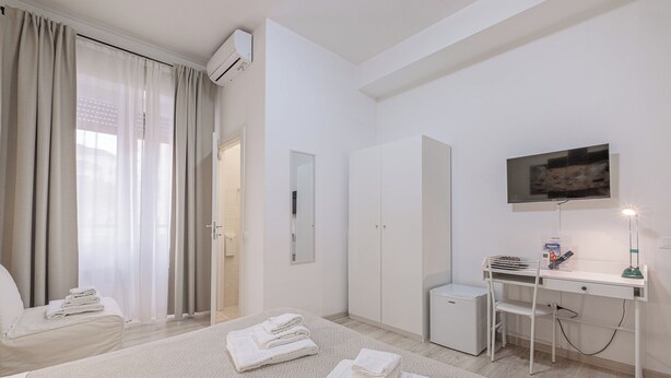 Quarto de hotel com cama, secretária, televisão e ar condicionado.