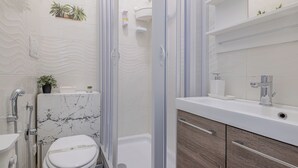 Um banheiro moderno com chuveiro em cabine de vidro, parede revestida em mármore, vaso sanitário branco e toucador de madeira com espelho.