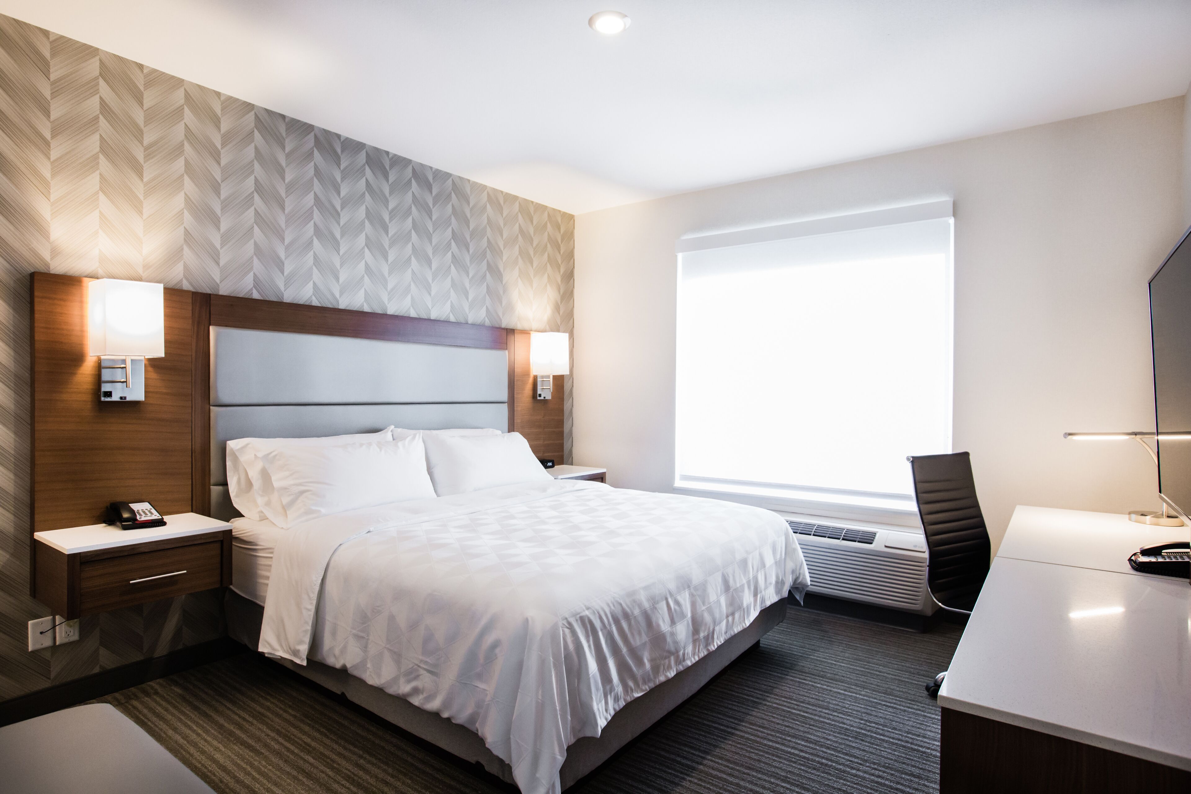 Quarto de hotel com uma cama grande, mesas de cabeceira, uma escrivaninha e uma cadeira.