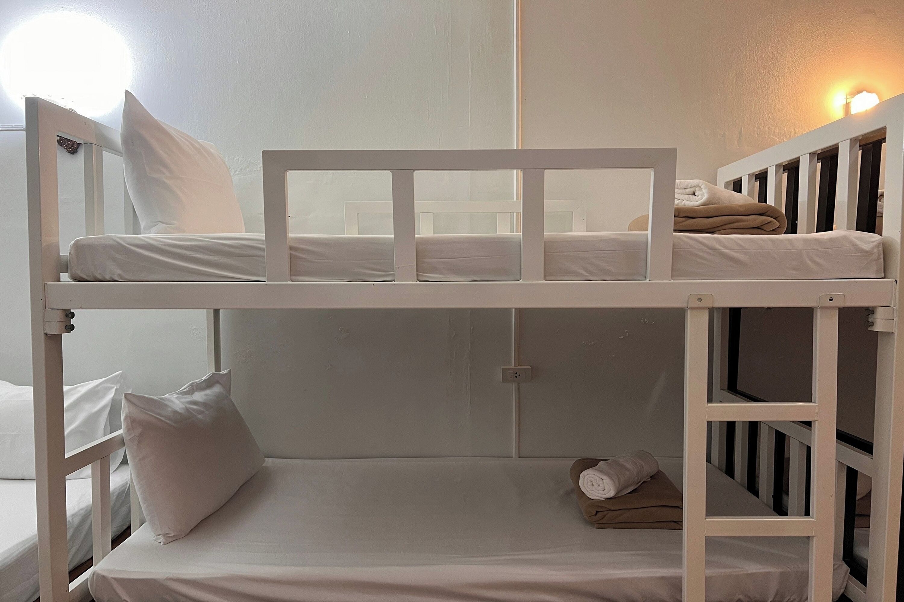 Quarto com beliches, roupa de cama branca e uma toalha pequena na cama inferior.