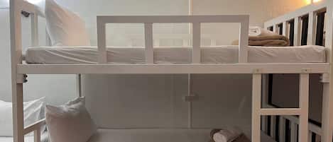 Quarto com beliches, roupa de cama branca e uma toalha pequena na cama inferior.