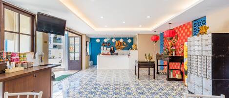 Um saguão de hotel com balcão de recepção, uma televisão e piso estampado.