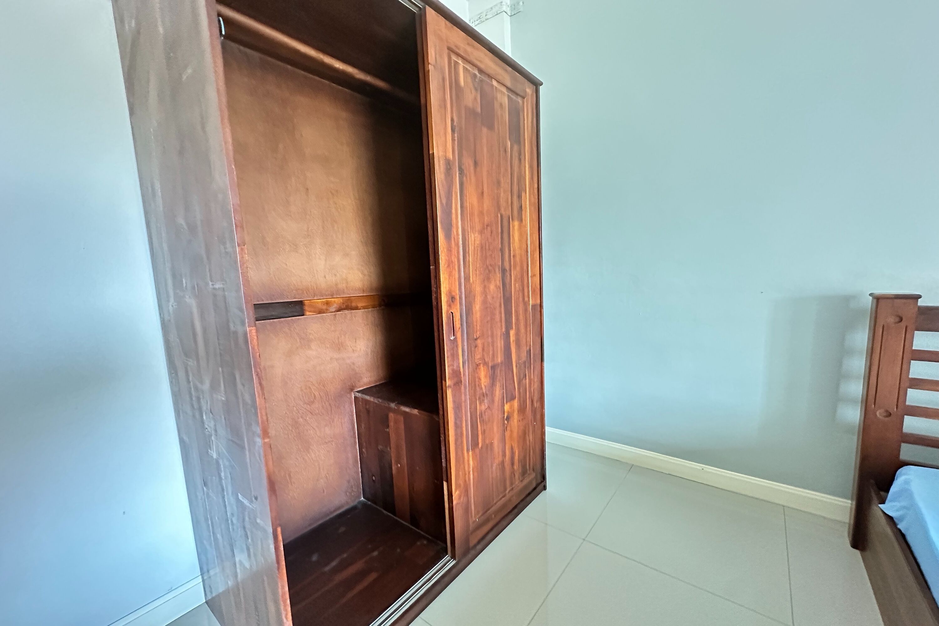 Quarto com guarda-roupa de madeira, uma cama e chão de azulejos.