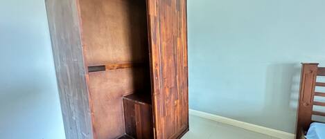 Quarto com guarda-roupa de madeira, uma cama e chão de azulejos.