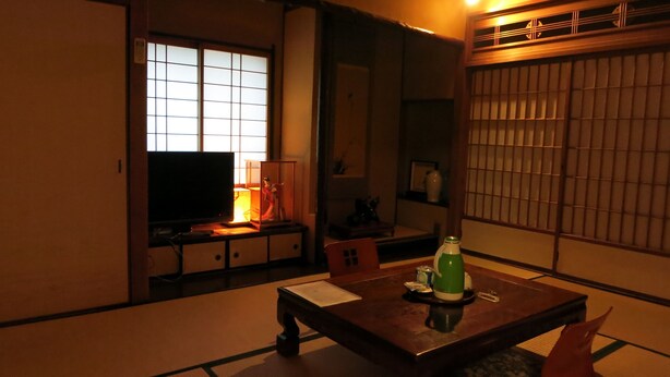 Um quarto japonês tradicional com tatames, uma mesa baixa com uma garrafa verde, uma televisão e portas deslizantes.