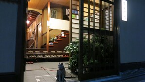 Interior japonês tradicional com um gato na coleira, uma escada e vista através de uma porta de madeira com treliça.