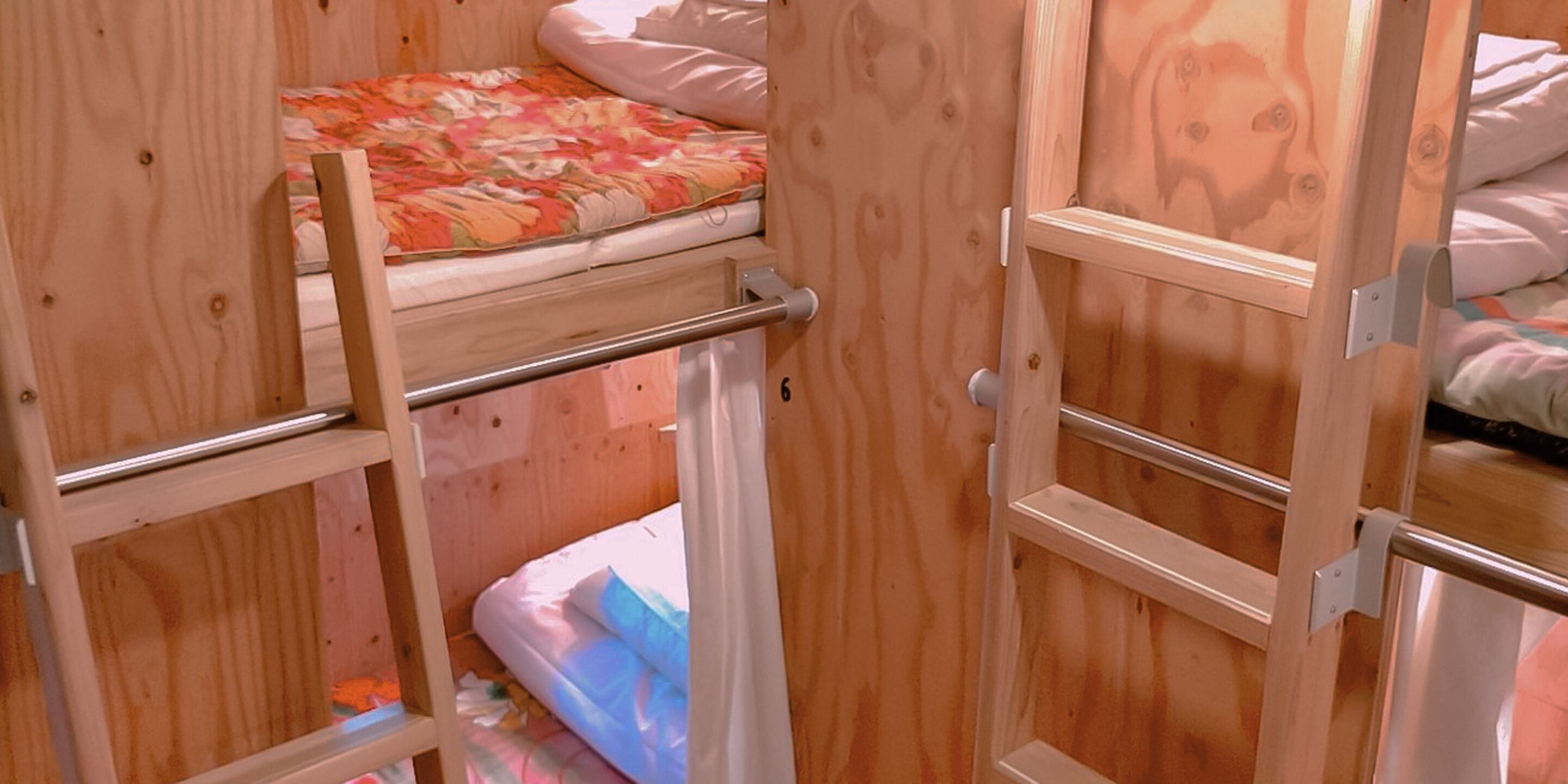 Uma cama beliche de madeira com escada retrátil, um colchão com padrão floral colorido e um travesseiro branco.