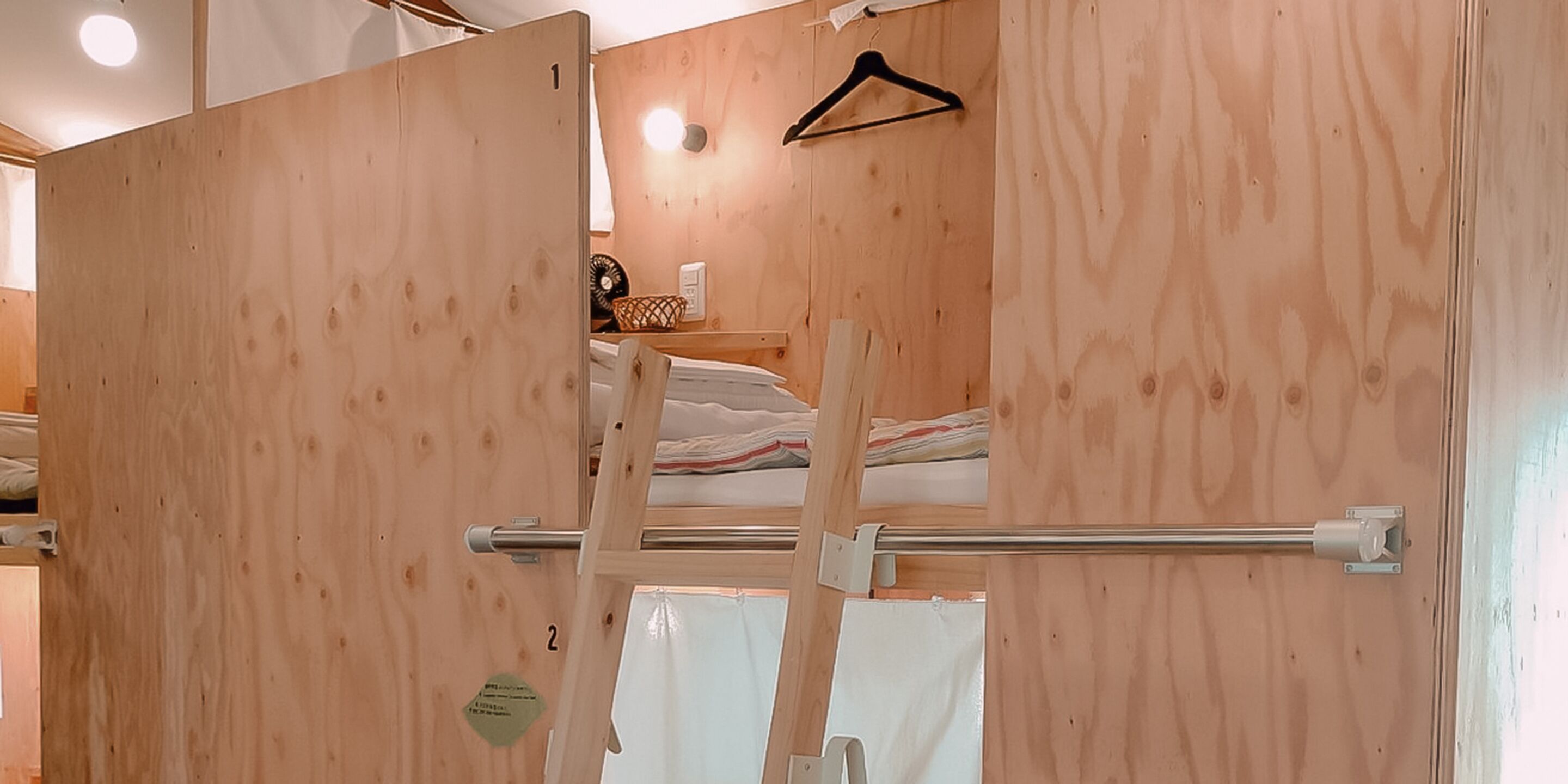 Quarto com beliche de madeira, escada, cabide preto pendurado e prateleira pequena com cesta.