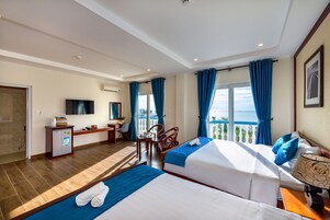 Quarto de hotel com duas camas, uma mesa, uma televisão e varanda com vista.