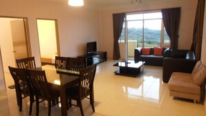 Uma sala de estar com mesa de jantar, cadeiras, sofá, televisão e varanda com cortinas.