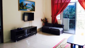 Uma sala de estar com televisão de tela plana, móvel de entretenimento preto, sofá escuro, cortinas vermelhas e uma varanda com vista para áreas verdes.