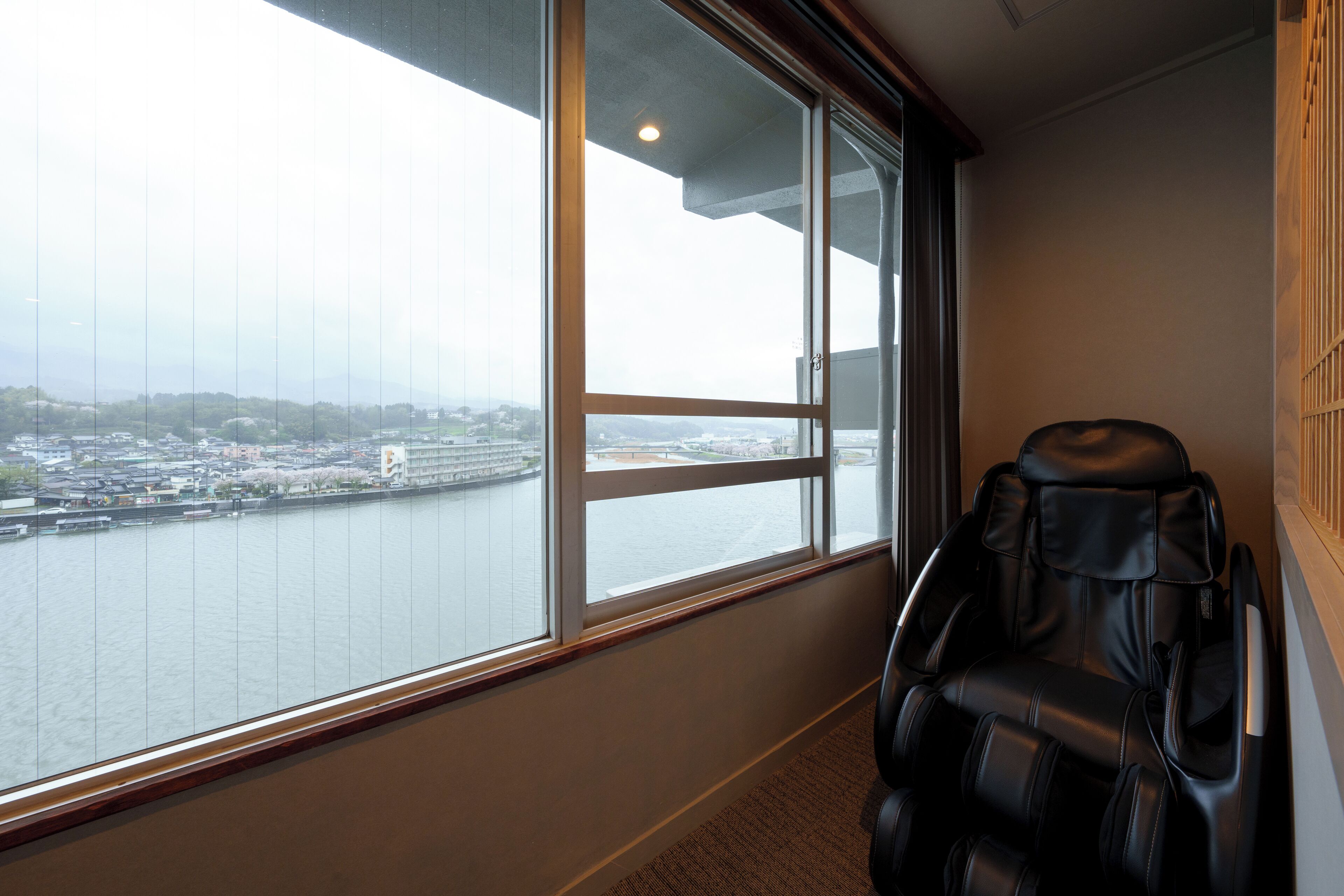 Uma cadeira de massagem perto de uma janela ampla com vista para um rio e edifícios.