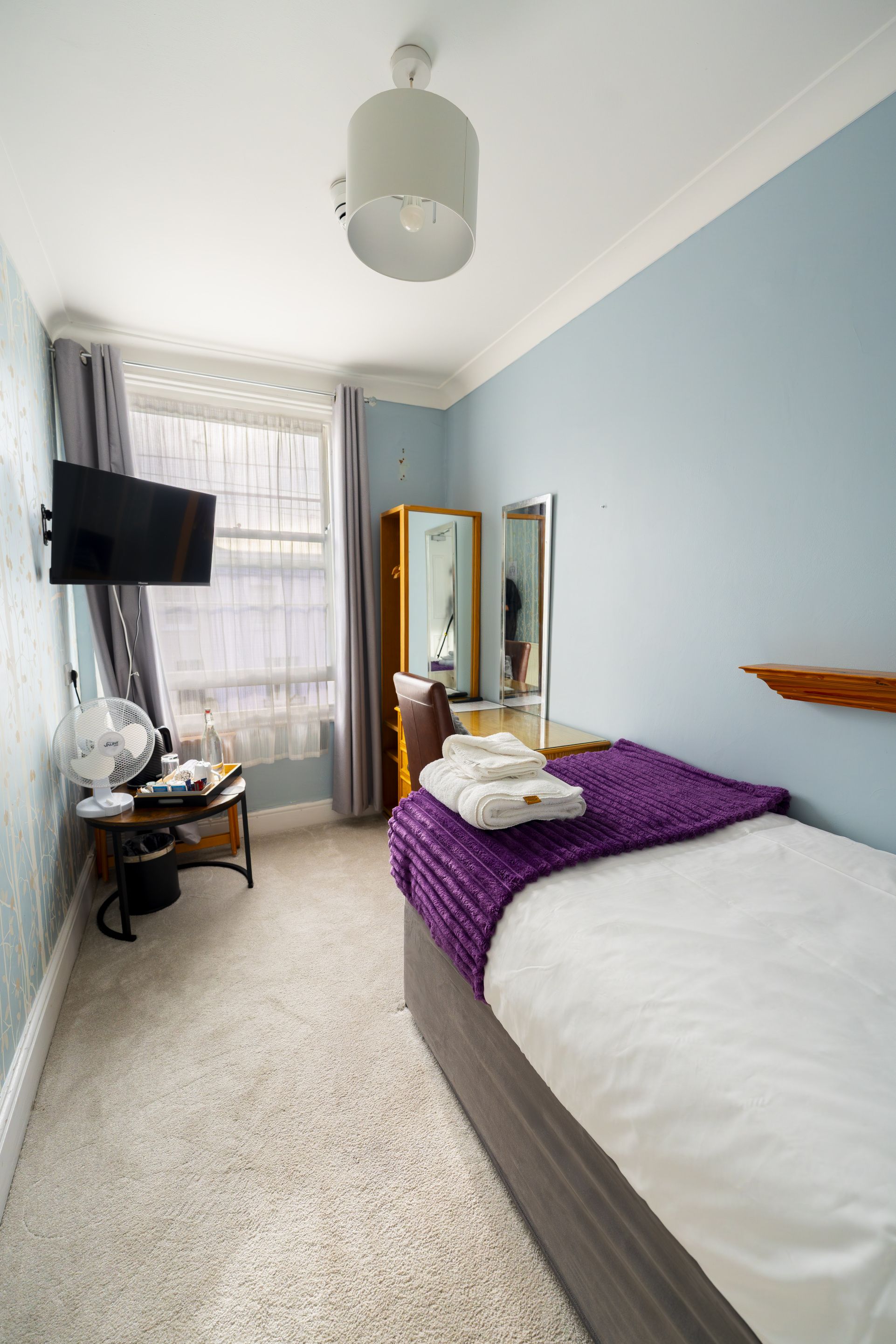 Quarto de hotel com cama, televisão de tela plana, escrivaninha com cadeira, janela com cortinas e espelho.