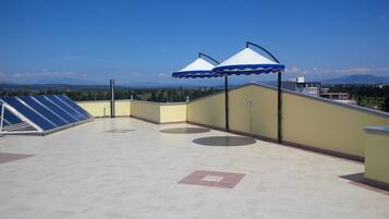 Terraço no telhado com painéis solares, dois guarda-sóis azul e branco e vista para montanhas distantes.
