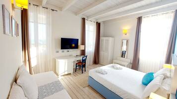 Quarto de hotel com cama, escrivaninha, cadeira, televisão e guarda-roupa.
